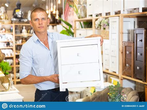 Portrait Of Attentive Man Choosing Chest Of Drawers In Furniture Store