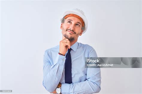고립 된 배경 위에 계약자 안전 헬멧을 쓰고 있는 젊은 사업가가 턱에 손을 얹고 질문 펜시브 표현을 생각하고 있습니다 사려 깊은 얼굴로 미소 의심 개념 건축가에 대한 스톡