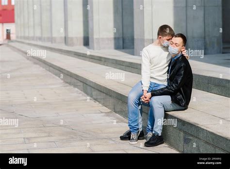 Young Gay Couple Wearing Medical Mask Hugging And Kissing At City