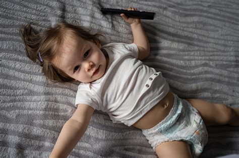 한 작은 백인 소녀 유아가 집 꼭대기보기에서 침대의 기저귀에 누워 원격 컨트롤러 복사 공간을 확보합니다 12 17 개월에 대한 스톡 사진 및 기타 이미지 Istock