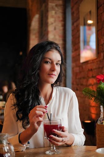여자는 커피 숍에서 멀드 와인을 마신다 흰색 셔츠와 레스토랑 카페에서 알코올 레드 와인 한 잔을 들고 손톱에 적갈색 바니시에 세련된 소녀 곱슬 머리에 대한 스톡 사진 및