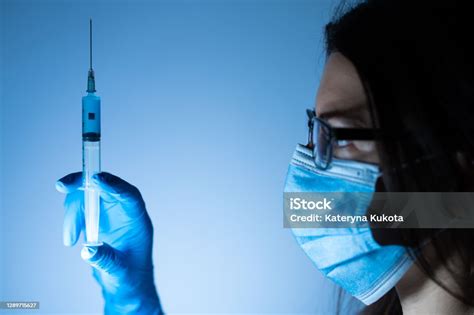 의료 용 마스크와 장갑을 낀 젊은 여성 의사는 코로나 바이러스 백신과 백신 칩이있는 주사기를 보유하고 있습니다 음모 이론 치핑