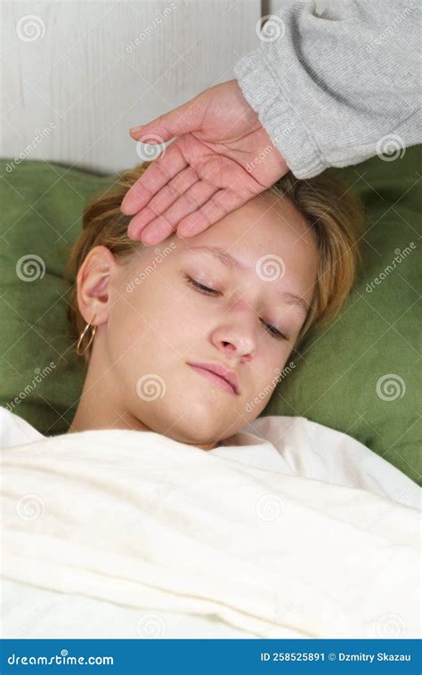 Mom Touches Her Hand To The Forehead Of A Sick Daughter Lying On The