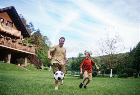 Dad Having Fun With Young Son Playing Football Running And Kicking