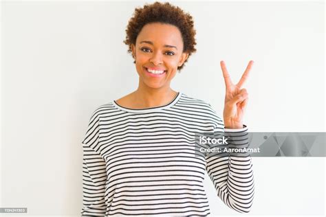 흰색 배경 위에 줄무늬 스웨터를 입고 있는 젊은 아름 다운 아프리카계 미국인 여자 표시 하 고 자신감과 행복 웃는 동안 두 손가락 번호를 가리키는 가리키기에 대한 스톡 사진