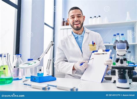 Hispanic Man Working At Scientist Laboratory Holding Blank Clipboard