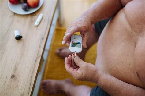 Overweight Man Checking Blood Glucose Level At Home Using A Fingerstick Glucose Meter The