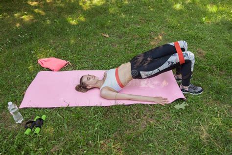 Pretty Woman In Sportswear Does Pelvic Lift On Green Lawn Grass Stock