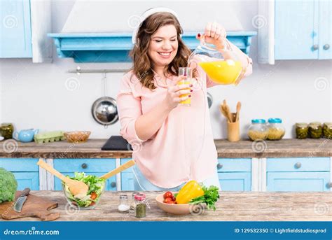 Smiling Overweight Woman In Headphones Pouring Juice Into Glass Stock