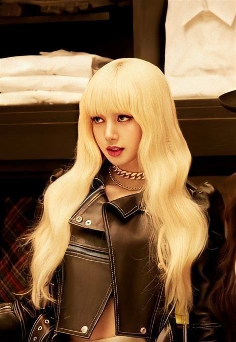 A Woman With Blonde Hair Wearing A Black Leather Jacket And Skirt Sitting In Front Of A Bed