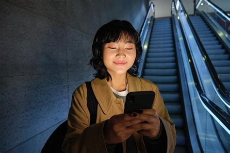 Retrato De Uma Linda E Feliz Garota Asiática Parada Com Smartphone Na