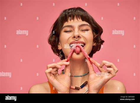 Pleased And Young Woman With Nose Piercing Licking Sweet And Sour Candy