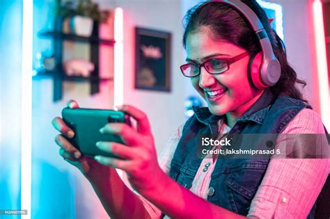 집에서 휴대 전화에서 온라인 비디오 게임을하는 헤드폰과 안경을 가진 행복한 웃는 소녀 라이브 스트리머 거룩한 날과 사이버 공간의 개념 인도 인도아 대륙에 대한 스톡 사진 및