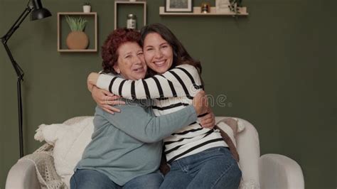 Grandmother And Granddaughter Joyfully Hugging Sitting On The Sofa In