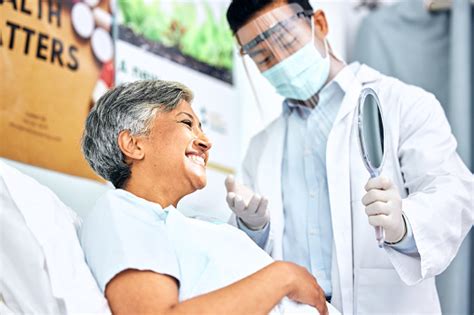 마스크를 쓴 치과 의사 미소와 치아 청소 청소 및 위생을 위한 거울을 가진 환자 의자에 행복한 여자 치과 치료 기술자 및 구강