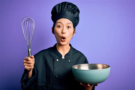 밥솥 유니폼과 모자를 쓰고 그릇을 사용 하 여 충격에 겁을 주는 젊은 아름 다운 중국 요리사 여자 두려움과 흥분 요리사에 대한