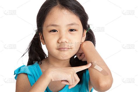 一个亚洲小女孩指着她手臂上的绷带