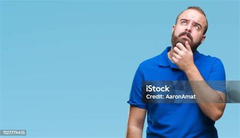 젊은 백인 소식통 남자 턱에 손으로 고립 된 배경 위에 파란 셔츠를 입고 질문에 대 한 생각 잠겨있는 표현 사려 깊은 얼굴로 웃 고 있습니다 의심의 개념입니다 남자에 대한