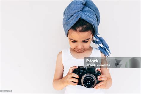 흰색 배경에 고립 된 사진 카메라를 들고 머리에 터번을 입고 귀여운 소녀의 이미지 흰색 배경에 포즈를 취하는 전문 카메라로