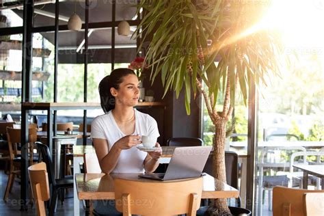 Young Beautiful Girl Sitting At A Table In A Cafe By The Window