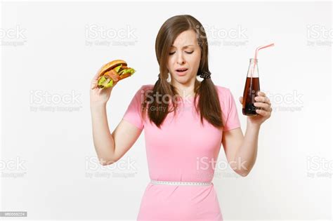 측정 테이프 햄버거 유리 병에 콜라를 들고 허리에서 꼬리 슬픈 젊은 여자는 흰색 배경에 고립 적절 한 영양 섭취 또는 고전적인