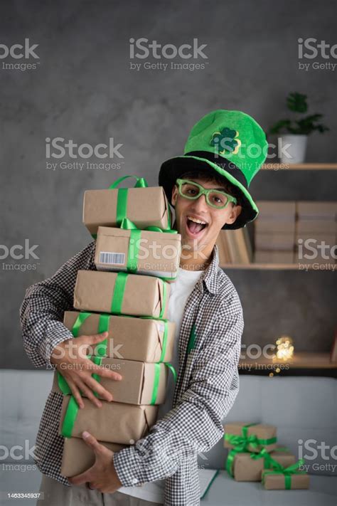 흥분한 재미있는 아랍 남자는 성 패트릭의 날을 축하하는 많은 선물 상자를 들고 카메라를 바라보며 레프러콘 모자를 쓰고 있습니다 성 패트릭의 날에 쇼핑 세일을 선물합니다 St
