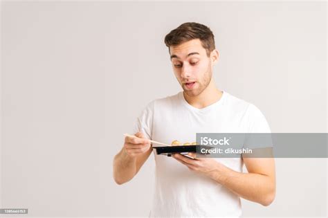 잘 생긴 젊은 남자의 초상화 흰색 고립 된 배경에 젓가락신선한 맛있는 초밥 롤을 먹는 남자에 대한 스톡 사진 및 기타 이미지