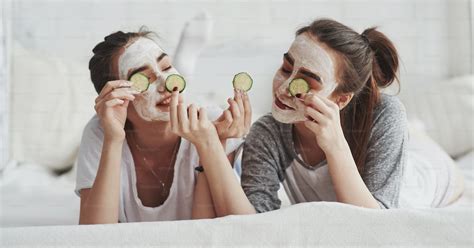 Whte 침대에 누워 얼굴에 신선한 오이 링과 흰색 마스크를 사용하여 피부 관리의 개념 두 여자 자매는 침실에서 주말을
