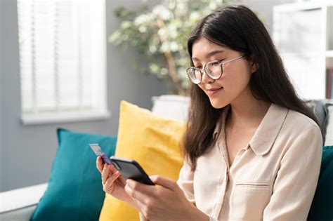 아시아 아름다움의 쇼핑 중독자는 소파에 거실에 손에 그녀는 전화와 은행 카드 신용 카드를 보유하고 여자는 온라인으로 구매를