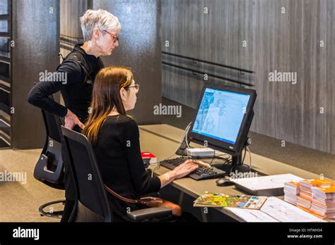 Two Female Librarians At Work Behind Computer Screen In Public Library