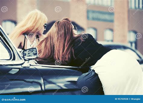 Two Young Fashion Women Leaning On Vintage Car In City Street Stock