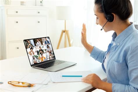 헤드셋을 낀 자신감 넘치는 백인 사업가 여성이 화상 회의 중 노트북 화면을 통해 다인종 동료들에게 손으로 인사하고 화상 통화로