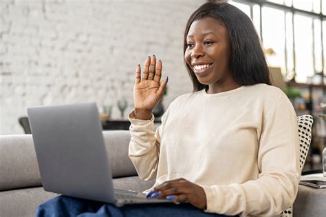 친구와 가상 회의 화상 통화 아름다운 다인종 소녀는 아늑한 소파에 노트북과 함께 앉아 노트북에 누군가에게 손을 흔들 가상현실에 대한 스톡 사진 및 기타 이미지 Istock