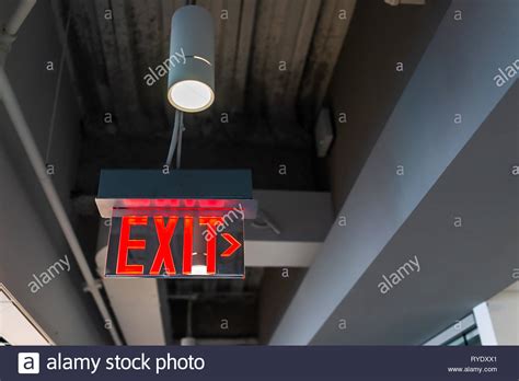Red Exit Sign Hanging From Ceiling Looking Up View With Arrow Direction And Color Illuminated