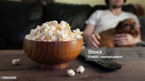 나무 테이블에 소금에 절인 팝콘과 Tv 리모컨 나무 그릇 배경에 소파에 Tv를 보고 빨간 개를 가진 남자 Premiere에 대한