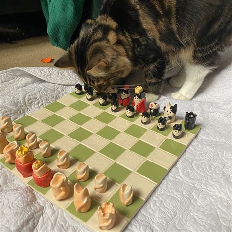 A Cat Sitting On Top Of A Table Next To A Chess Board And Game Pieces