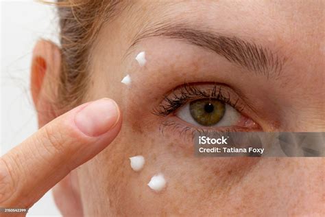 피부에 크림을 바르는 카메라를 보고 있는 중년 백인 여성의 자른 눈을 클로즈업합니다 보습제에 대한 스톡 사진 및 기타 이미지