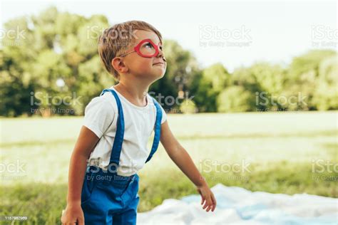 푸른 반바지와 빨간 종이 안경을 쓰고 자연 배경에서 놀고있는 어린 소년 공원에서 녹색 잔디에서 놀고있는 쾌활한 아이 야외에서