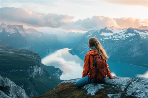 A Woman Is Seen Sitting On Top Of A Mountain Gazing At A Lake In The