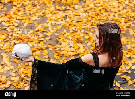 Brunette Woman In Black Goth Dress Holding Human Skull In Reaching Hand