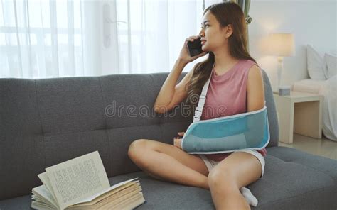 Young Asian Woman Wearing Soft Splint Due To Sore Arm Using Phone On