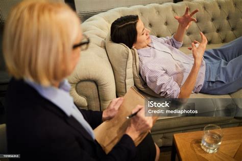 소파와 몸짓 손에 누워 캐주얼 셔츠에 화가 젊은 여자 치료사에 그녀의 감정을 설명 하는 동안 여자 정신과 의사 만들기 노트