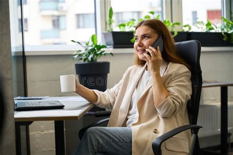 Beautiful Young Woman Sitting In Office Chair With Mobile Phone Stock