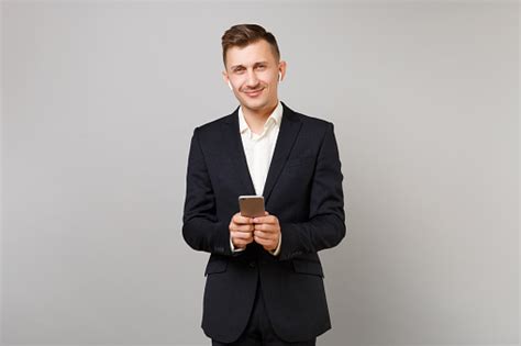 젊은 사업가 음악 휴대 전화를 사용 하 여 무선 이어폰 웃 고 회색 배경에 고립 Sms 메시지를 입력 성과 경력 부 비즈니스