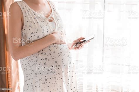 집에서 창과 문자 메시지 옆에 서 꽤 젊은 임신 한 여자 25 29세에 대한 스톡 사진 및 기타 이미지 25 29세 가정의