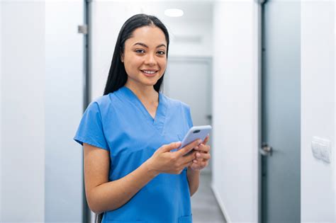 제복을 입은 미소 짓는 아시아 여성 치과 직원 스마트폰을 사용하여 현대 치과 진료소의 복도에 서 있습니다 30 34세에 대한 스톡 사진 및 기타 이미지 Istock