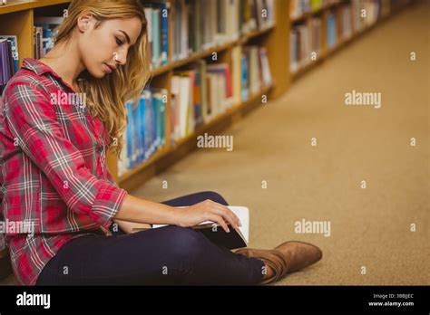 sitting woman reading open book on lap in library aisle leaning