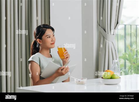 Young Asian Woman Reading Book Drinking Orange Juice At Home Stock