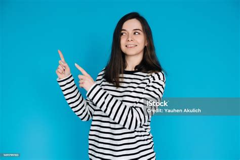 줄무늬 풀오버를 입은 사랑스러운 소녀가 빈 공간을 가리키고 응시하고 있다 표현적인 제스처를 가진 매력적인 젊은 여성 모델 파란색 배경에 격리 개념 광고에 적합 30 34세에