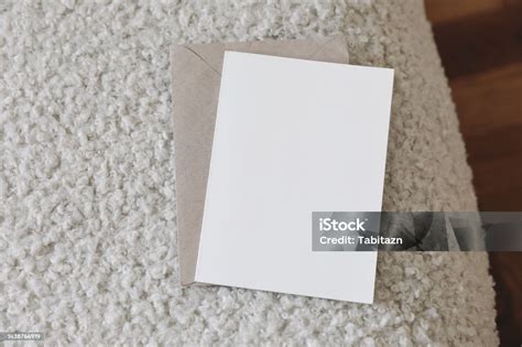 중립 문구 정물 장면 빈 인사말 카드 초대장 모형 및 흰색 Boucle 소파 실내 장식에 공예 봉투 테디 질감의 원단 흐릿한